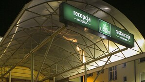 Entrada de hotel com área de recepção, escada e carros estacionados.