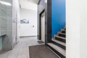 Um corredor com piso de mármore, parede azul e escada com corrimão preto.