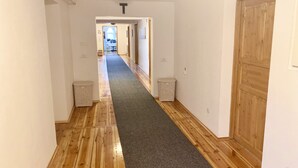 Um corredor com piso de madeira, carpete escuro e uma porta de madeira à direita.