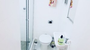 Casa de banho moderna com cabine de chuveiro em vidro, sanita branca e lavatório com um frasco de sabonete verde.