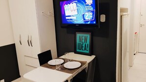 Uma área de refeições com uma mesa posta para dois, uma televisão fixada na parede e um aviso que diz "NOVA IDEIA!"