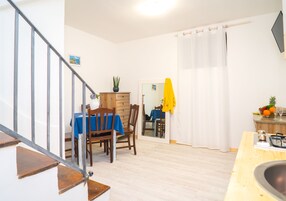 Uma área de refeições com uma mesa e cadeiras de madeira, uma escada e uma cozinha com pia e bancada.