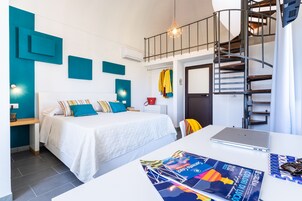 Quarto de hotel moderno com uma cama, uma escrivaninha com um laptop e uma escada em espiral.