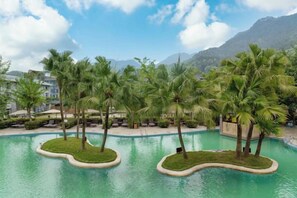 Área de piscina com palmeiras e montanhas ao fundo.