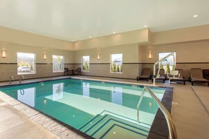 Uma grande piscina interna com água cristalina, rodeada por espreguiçadeiras e janelas com vista para o exterior.