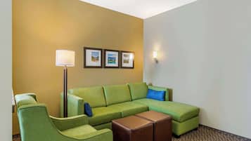 Um sofá verde, uma mesa pequena e um abajur em um quarto de hotel.