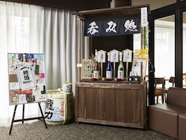 Quarto com área de bar de madeira exibindo diversos frascos, um mural com papéis e uma placa tradicional japonesa.