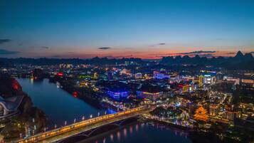 Paisagem urbana ao entardecer com edifícios iluminados, um rio e uma ponte.