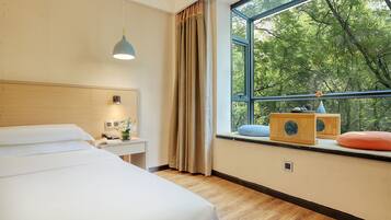 Quarto de hotel com cama, mesa de cabeceira, abajur, janela com cortinas e vista para árvores.