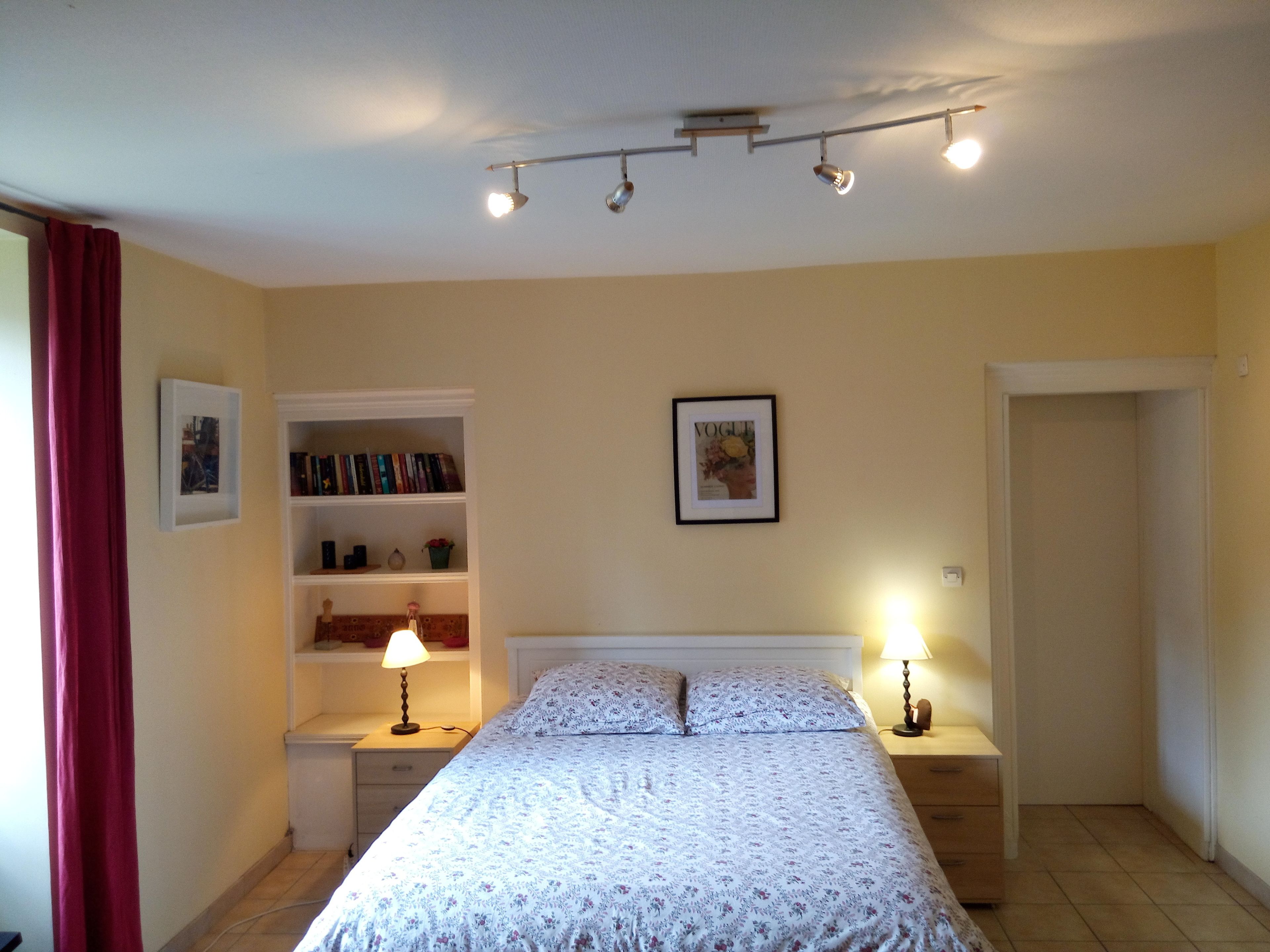 Quarto com cama, mesas de cabeceira, estante e porta.