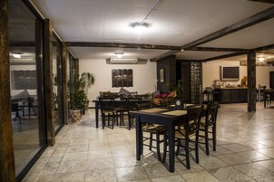 Uma sala de jantar ampla com uma mesa grande e cadeiras, uma planta em vaso e um ventilador de teto.
