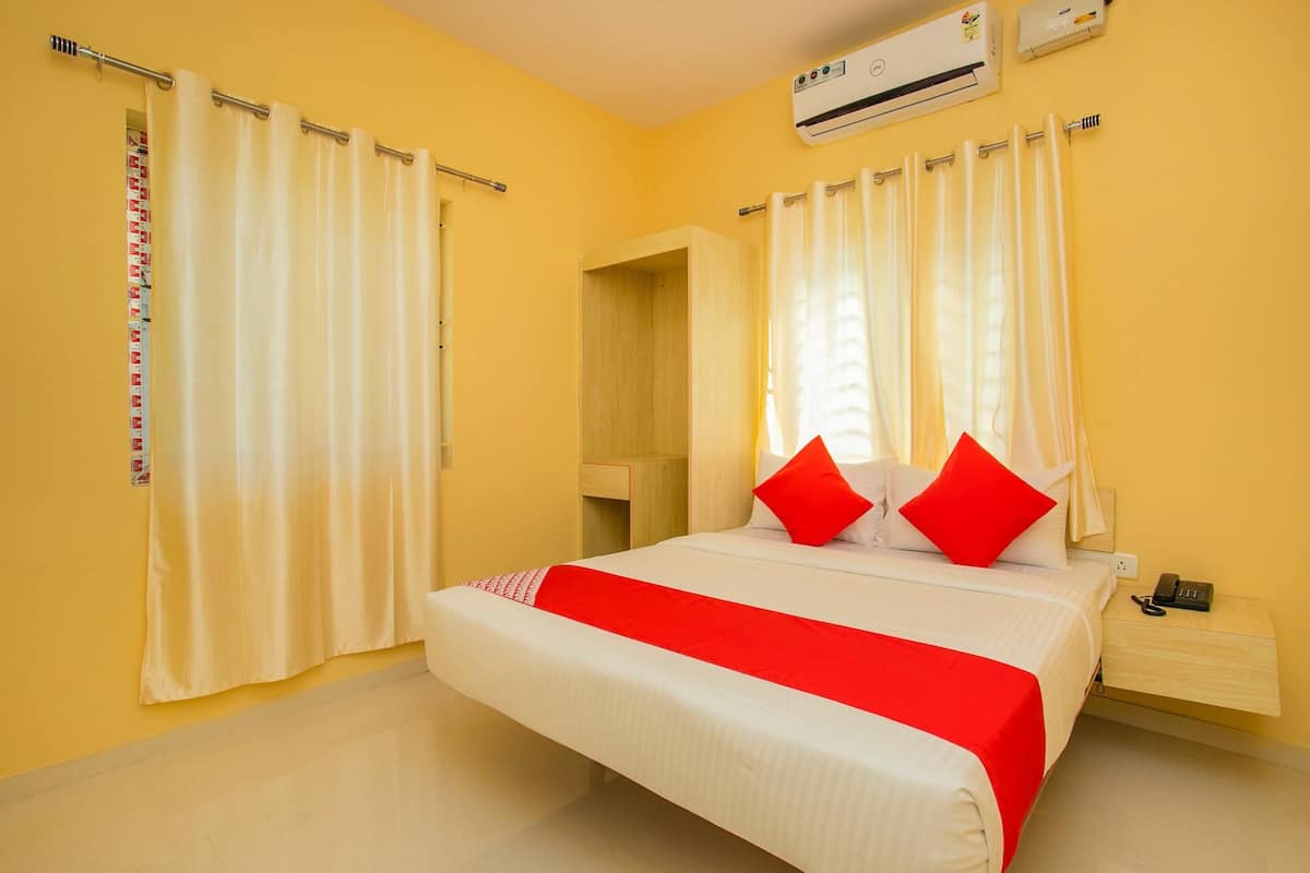 Quarto de hotel com cama, cortinas, aparelho de ar condicionado, mesa de cabeceira com telefone e um pequeno espelho.