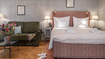Quarto de hotel com uma cama, um sofá verde, uma mesinha com um vaso de flores e duas quadros na parede.