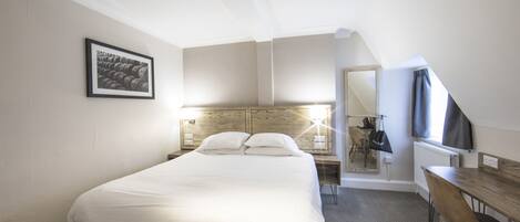 Quarto de hotel bem arrumado com cama grande, escrivaninha, cadeira, espelho e quadro na parede.