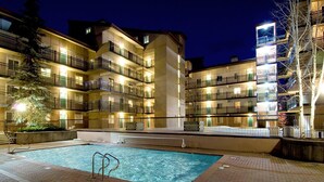 Piscina com deck azulejado, cercada por edifícios altos com sacadas e iluminação externa.