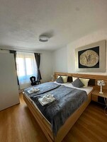 Uma cama de casal com cabeceira de madeira, uma mesinha de cabeceira com abajur e uma obra de arte emoldurada na parede.