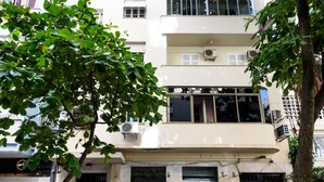 Um edifício com várias andares, varandas, aparelhos de ar condicionado e uma árvore em primeiro plano.