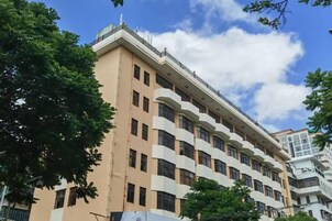 Um edifício com vários andares, fachada bege, múltiplas varandas e céu claro com nuvens.