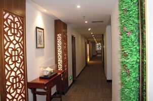 Corredor de hotel com painéis de madeira decorativos, um balcão de recepção e uma parede verde com plantas.