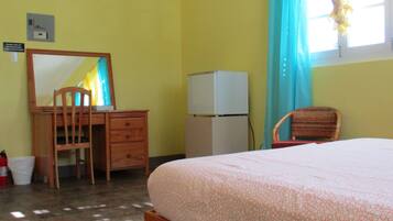 Quarto com cama, escrivaninha, cadeira, espelho e janela com cortinas.