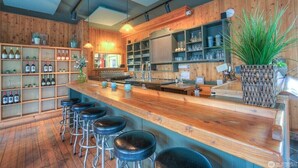 Uma área de bar com prateleiras de madeira, banquetas e um balcão.