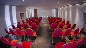 Uma sala de conferências com fileiras de cadeiras vermelhas e piso escuro.
