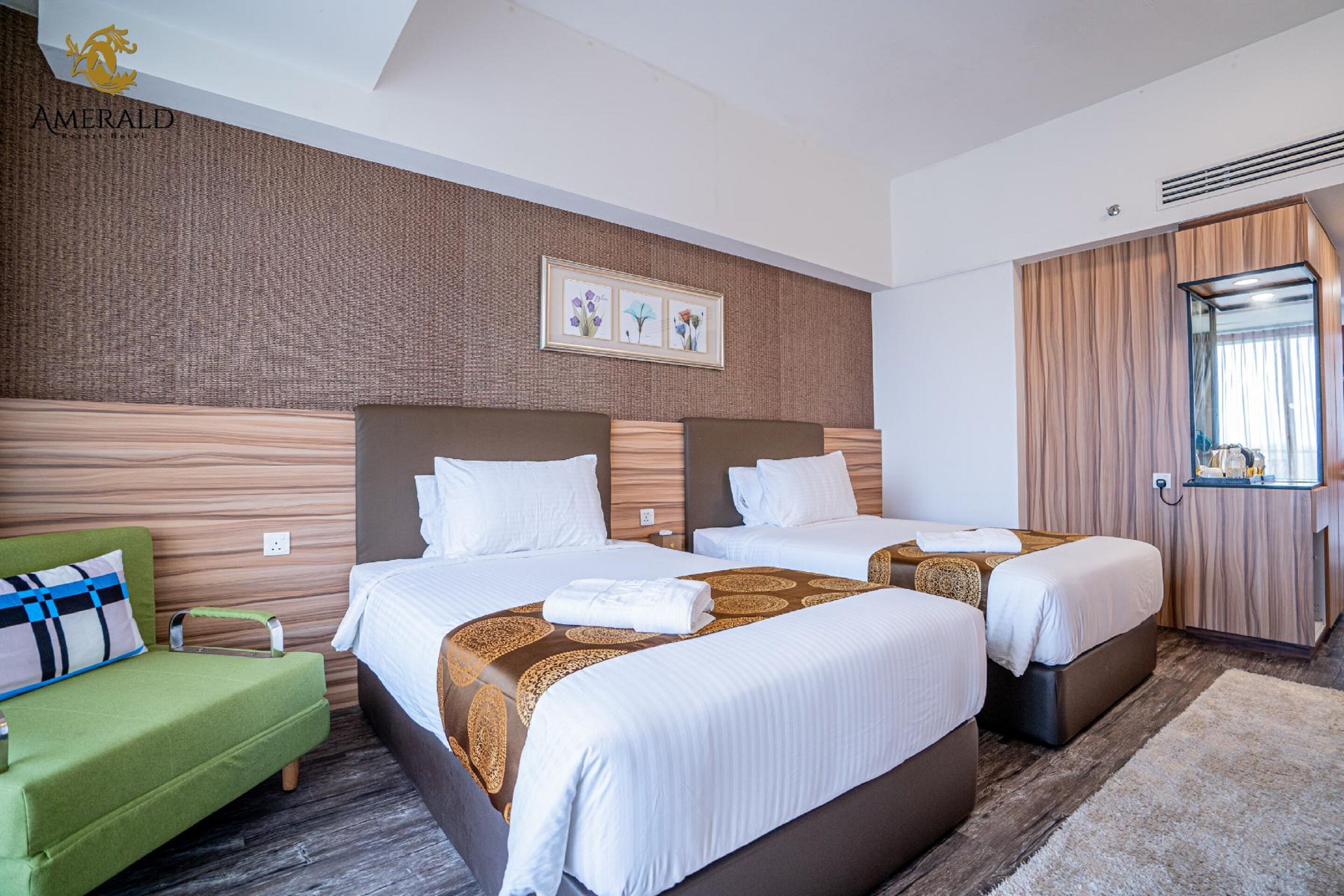 Quarto de hotel com duas camas, uma poltrona verde, cabeceira de madeira e um quadro na parede.