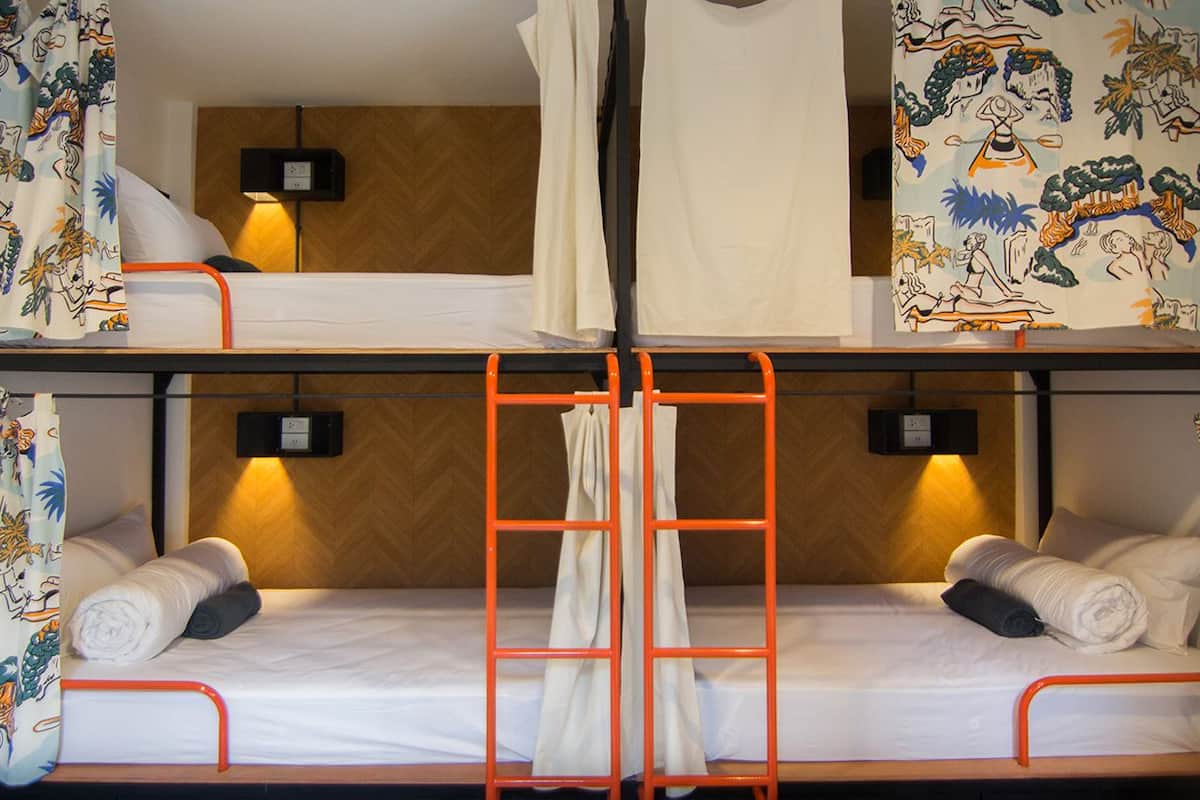 Quarto com beliches, duas camas, cada uma com cabeceira, escada e luminária fixada na parede.