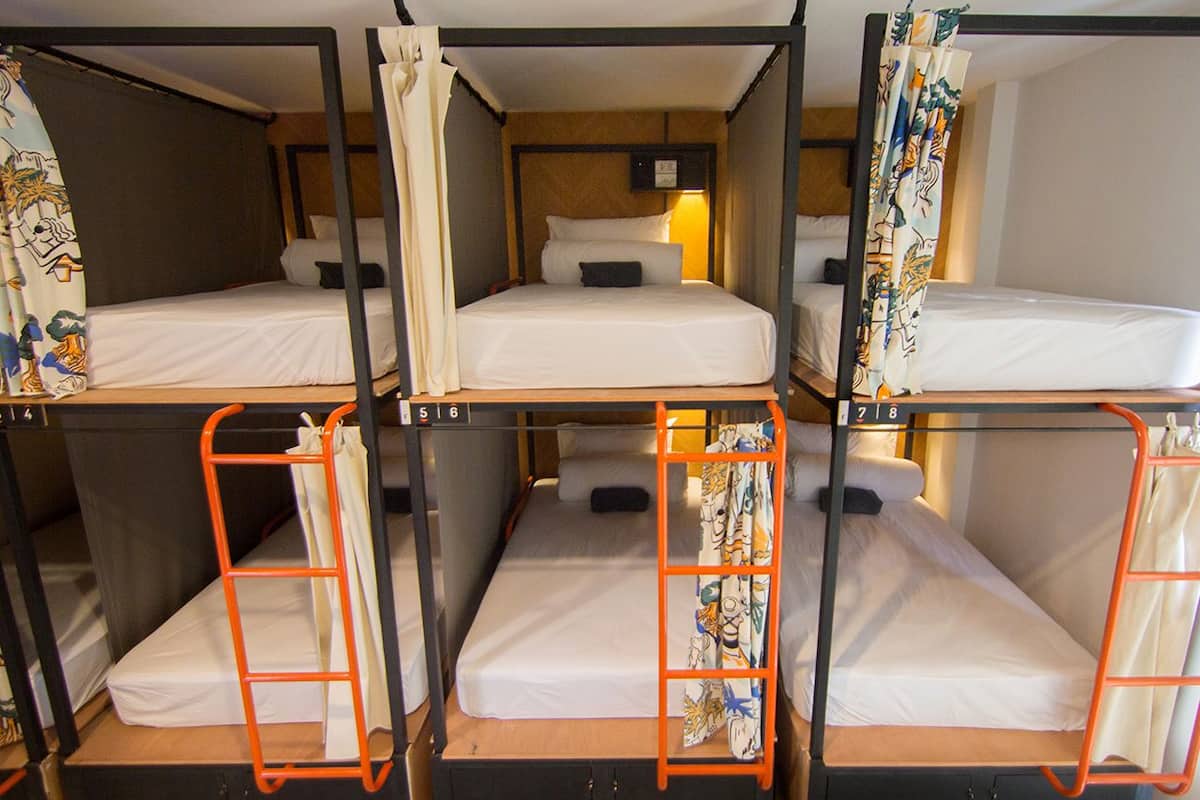 Quarto com beliches, três camas, cada uma com cortina e escada.