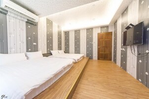 Quarto de hotel com duas camas, piso de madeira, televisão presa na parede e porta de madeira.