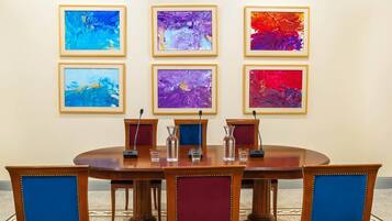 Uma sala de conferências com uma mesa redonda, seis cadeiras e seis quadros abstratos emoldurados na parede.