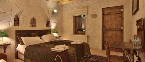 Quarto com cama, cadeira de madeira, mesa, abajur, radiador e porta.