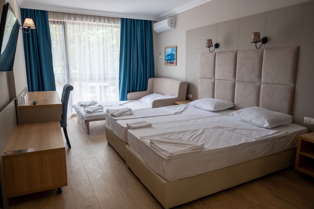 Quarto de hotel com uma cama grande, uma escrivaninha, uma cadeira e uma janela com cortinas.