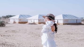 Uma pessoa de vestido branco em um deserto, com tendas brancas ao fundo.