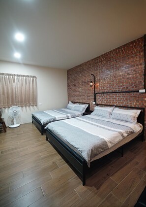 Quarto com duas camas, parede de tijolos, ventilador de teto e janela com cortinas.