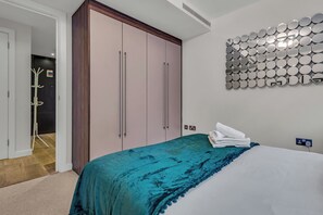 Quarto com cama, manta verde-água, espelho fixado na parede e guarda-roupa.