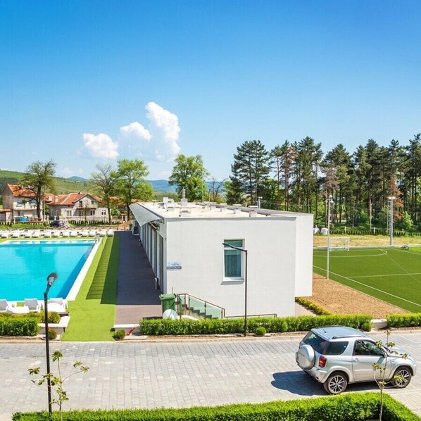 Um edifício moderno com piscina, campo esportivo e área de estacionamento.