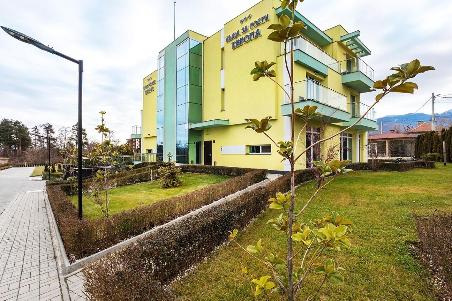 Um edifício moderno com fachada amarela e detalhes verdes, exibindo uma placa em idioma estrangeiro.