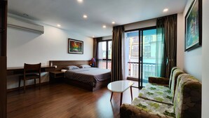 Quarto de hotel moderno com cama, escrivaninha, cadeira, sofá e uma varanda com cortinas.