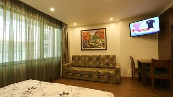 Quarto de hotel com cama, sofá, televisão e um quadro na parede.