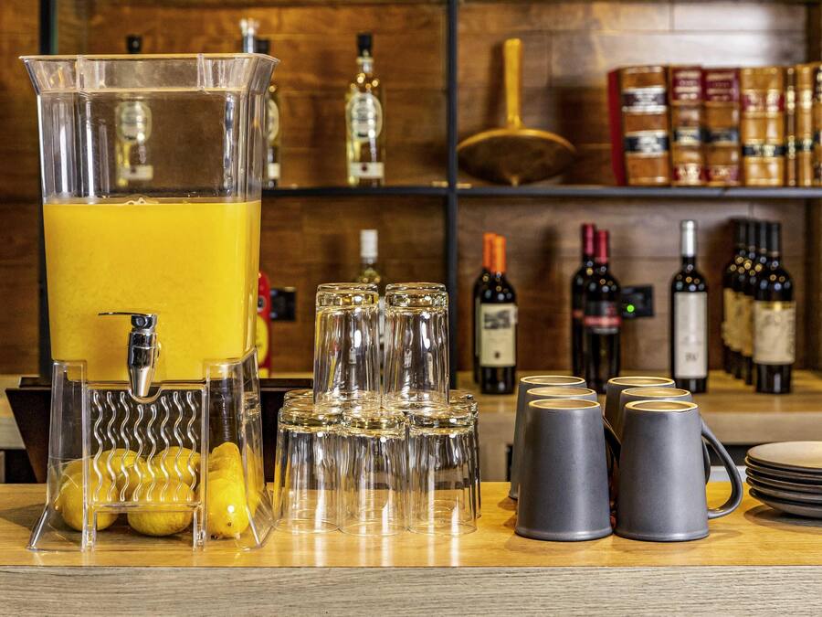 Uma área de bar com um jarro grande, copos, limões e garrafas de bebidas alcoólicas.