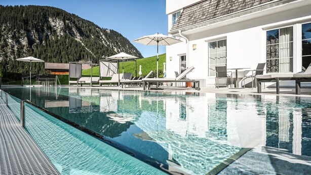 Piscina com espreguiçadeiras e guarda-sóis, emoldurada por uma paisagem montanhosa.