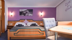 Quarto de hotel com cama, uma cadeira, uma mesa e parede com um quadro e duas arandelas.