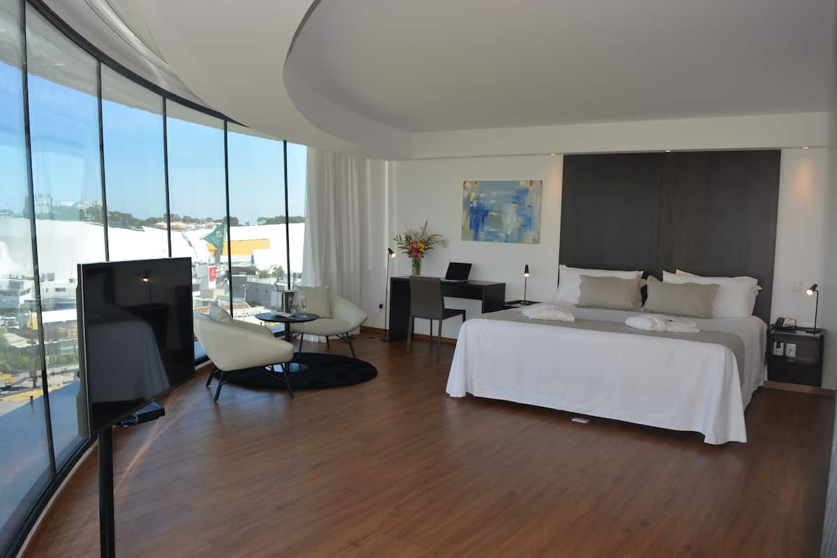 Quarto de hotel moderno com uma cama grande, escrivaninha, cadeira e televisão.