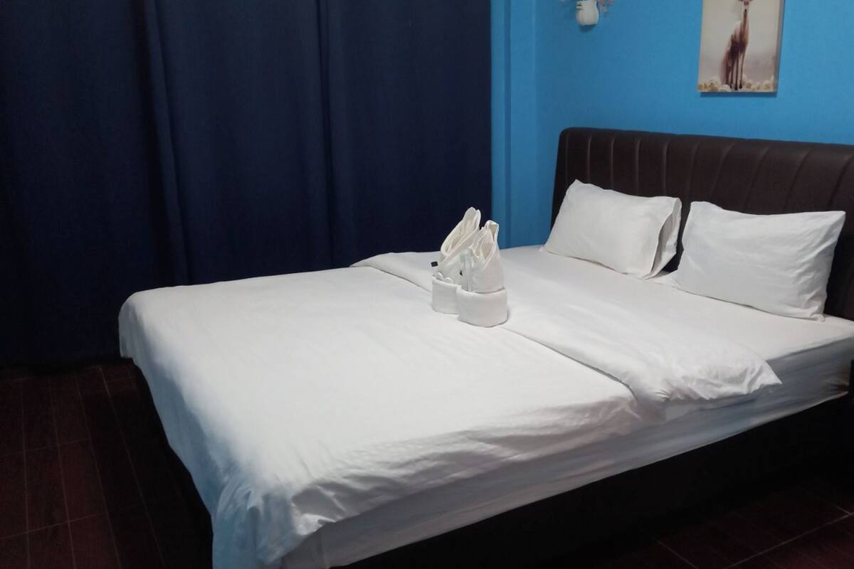Cama bem arrumada com lençóis brancos e um conjunto de toalhas brancas ao lado.