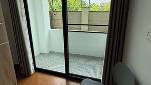 Quarto com porta de vidro deslizante que dá para uma varanda com grades de metal e um parapeito de concreto.