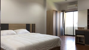 Quarto de hotel moderno com uma cama grande, cabeceira de madeira, escrivaninha com cadeira e uma janela ampla com cortinas.