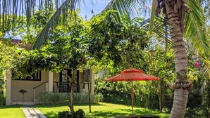 Um jardim bem cuidado com um caminho, palmeiras e um guarda-sol vermelho.