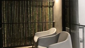Casa de banho moderna com parede de bambu, duas cadeiras brancas e uma janela grande.