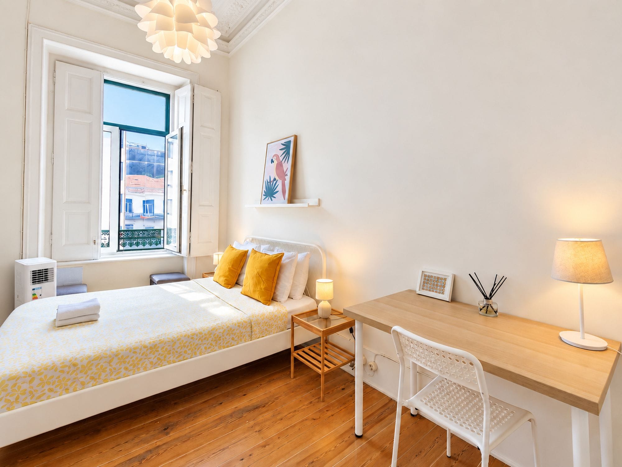 Quarto de hotel com cama, escrivaninha, cadeira, janela e prateleira fixada na parede com um quadro.